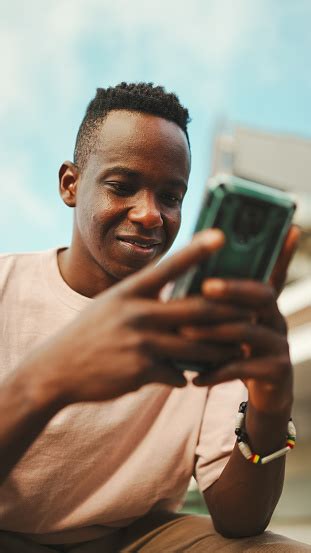 젊은 아프리카 학생은 대학 밖에 앉아서 휴대 전화를 사용하고 스마트 폰 화면을 탭합니다 25 29세에 대한 스톡 사진 및 기타 이미지 25 29세 T 셔츠 공부