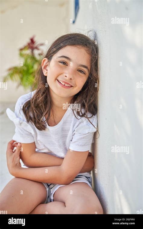 Adorable Cheerful Preteen Girl In T Shirt And Shorts Sitting On Street