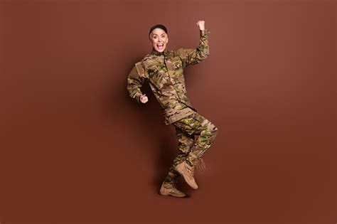 갈색 배경에 고립 된 옷을 입은 위장 육군 제복을 이기는 사랑스러운 연금 수령자 숙녀 전문 장교의 전체 길이 사진 60 64세에
