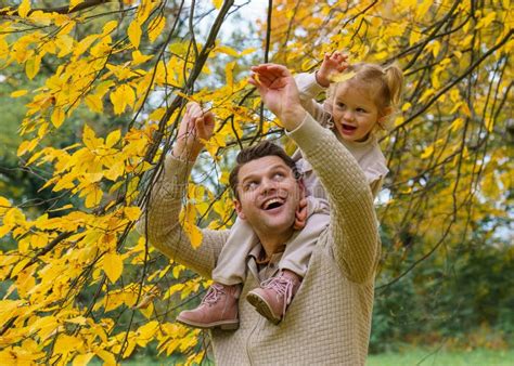 Joyful Father And Young Daughter Playing While Walking In Beautiful Autumn Park Girl Sitting On