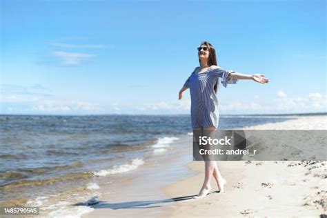 두 손을 벌리고 서 있는 바다 해변에서 자유로운 행복을 누리고 있는 행복한 미소 짓는 여자 여름 드레스를 입은 갈색 머리 여성 모델의 초상화는 야외 휴가 휴가 동안 자연을