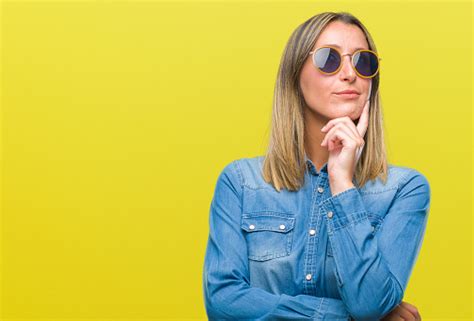 손으로 턱 질문 잠겨있는 표현에 대 한 생각에 고립 된 배경 위에 선글라스를 입고 젊은 아름 다운 여자 사려깊은 얼굴 미소 의심 개념입니다 금발 머리에 대한 스톡 사진 및