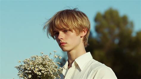 어깨까지 내려오는 금발 머리를 가진 젊은 남자의 초상화입니다 그는 흰색 칼라 셔츠를 입고 나무를 배경으로 파란 하늘 앞에 서 있습니다 남자는 진지한 표정으로 옆을