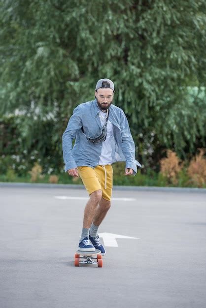 Premium Photo Young Stylish Hipster Man Riding Longboard On Street