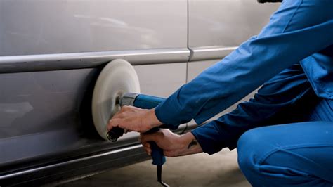 클로즈업 손 남성 정비사 착용 기계공의 유니폼은 작업 안전을 위해 앉아서 자동차 연마기 스크럽을 천천히 잡고 기계를 단단히 잡고 내려 가기 전에 자동차 표면을 매끄럽게