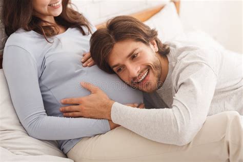 Future Dad Listening Belly Of His Pregnant Wife Lying On Bed Stock