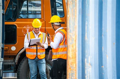 전문 엔지니어링 남성 노동자가 이야기하고 컨테이너 공장에 서 관리자는 내부 감사를 위한 검사 보고서 논문에 대해 논의합니다 제조에 대한 품질 보증 컨셉 엔지니어 운영 2명에