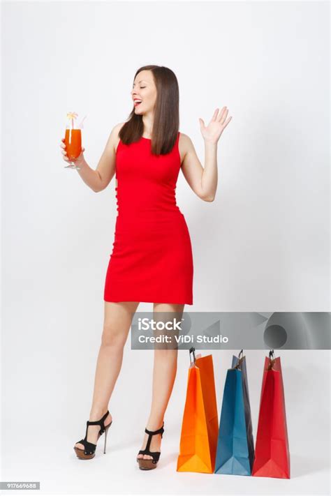 전체 길이 매력적인 매력적인 음료 칵테일 다중의 유리를 잡고 빨간 드레스의 젊은 여자 색 흰색 배경에 고립 된 쇼핑 후 구입 패킷을 광고에 대 한 공간을 복사 합니다 가방에