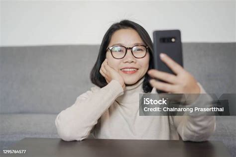 스마트 폰을 들고 있는 젊은 아시아 여성이 주말에 집 안의 거실에서 친구 및 가족과 소통하여 사회적 거리와 격리 시간 개념을 확보했습니다 40 44세에 대한 스톡 사진 및