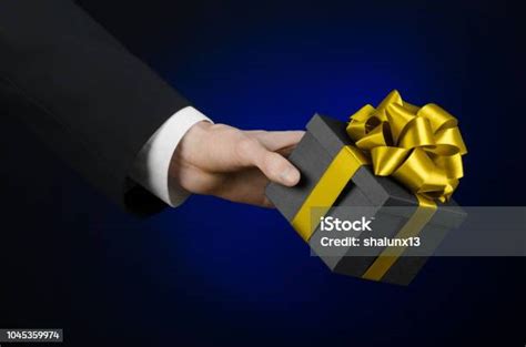 축 하와 선물의 테마 절연 스튜디오에 진한 파란색 배경에 골드 리본 아름 다운 블랙 박스에 포장 하는 독점적인 선물 비싼 선물을 들고 검은 양복에 남자 검은색에 대한 스톡