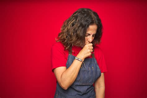 빨간 고립된 배경 위에 앞치마 유니폼을 입은 중년 노인 여성은 감기 나 기관지염의 증상으로 기분이 좋지 않고 기침합니다 헬스케어 개념 기침하기에 대한 스톡 사진 및 기타