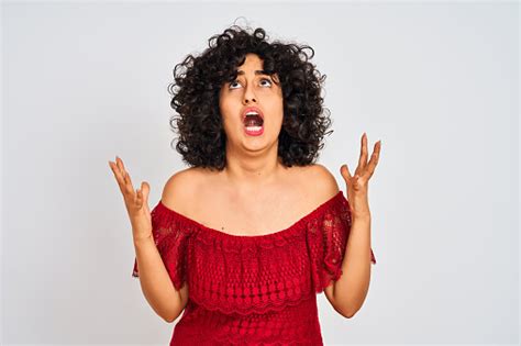 고립 된 흰색 배경 에 서 빨간 드레스를 입고 곱슬 머리를 가진 젊은 아랍 여성은 미친 미친 미친 소리와 공격적인 표정과 팔을 제기 고함 좌절 개념입니다 드레스에 대한 스톡