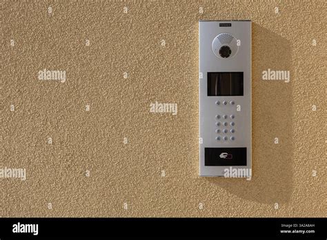 Modern Intercom System With Camera Keypad And Rfid Access On Textured Wall In Sunlight
