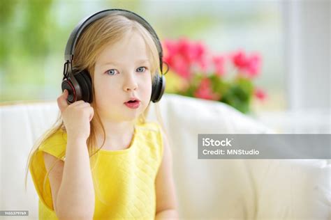 거대한 무선 헤드폰을 착용 하 고 귀여운 소녀입니다 음악을 듣고 있는 예쁜 아이 여학생은 집에서 아이들의 노래를 듣고 재미있게 놀고 있습니다 가정 생활에 대한 스톡 사진 및