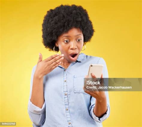 노란색 배경에 고립된 스튜디오에 있는 흑인 여성의 전화 놀라움과 충격 와우 핸드폰과 소셜 미디어 Omg 또는 Wtf 이모티콘에서 가짜 뉴스를 읽기 위해 스마트폰으로 놀란