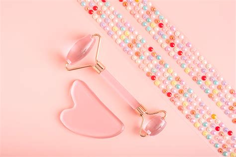 핑크 석영 스톤 롤러 페이셜 구아 샤 파스텔 핑크 배경에 라인 스톤 얼굴 트리트먼트 및 스파 천연 유기농 미용 제품 0명에 대한