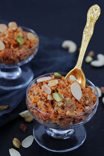 가자르 카 할와 달콤한 인도 디저트 푸딩 가당당근 그릇 캐슈와 피스타치오 너트 숟가락을 얹은 아몬드를 검은 소재 배경에 대고 있는 유리 그릇의 이미지 전경에 초점을 맞추고