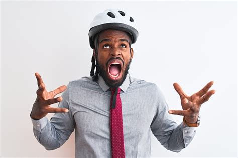 고립 된 흰색 배경에 자전거 헬멧을 쓰고 머리띠를 착용한 아프리카 계 미국인 사업가는 공격적인 표정과 팔을 들고 미친 소리와 고함을 지으며 좌절 개념입니다 땋은 머리에 대한