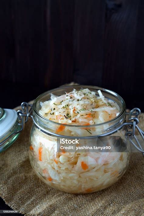 검은 색 배경에 유리 항아리에 허브와 당근과 수제 소금에 절인 양배추 나무 테이블에 자루가 있는 양배추절임 복사 공간을 복사합니다 수직 채식 음식 통조림 식품의 개념 0명에