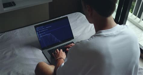 Digital Workspace Man Typing Programmer Code On Laptop Seated On Bed Rear View IT Freelancer