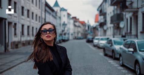 검은 코트와 선글라스를 쓴 여자가 길 한가운데에 서 있다 사진 Unsplash의 무료 폴란드 이미지