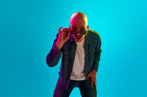 네온 불빛의 파란색 스튜디오 배경에 세련된 옷과 선글라스를 끼고 콧수염을 기른 젊은 대머리 남자의 초상화 20 24세에 대한 스톡 사진 및 기타 이미지 Istock