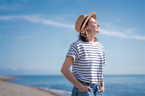 푸른 바다의 황량한 모래 해변을 따라 걷는 모자를 쓴 젊은 행복한 여자 여름 방학 및 여행 걷기에 대한 스톡 사진 및 기타