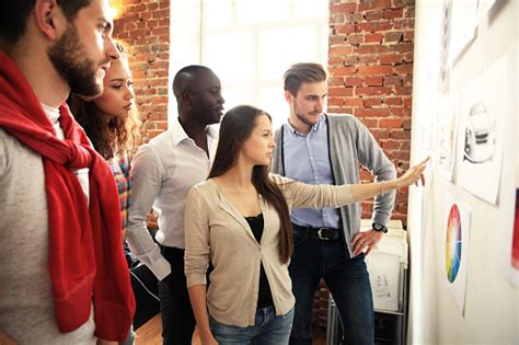 협업은 최상의 결과를 열쇠 이다 스마트 캐주얼 젊은 여자 Infographic 사무실에서 흰 벽에 표시를 가르키고 있는 동안 비즈니스 전략 수립에 현대 젊은이의 그룹 업무