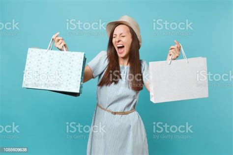 세로 행복 여름 패키지 가방을 들고 드레스 밀 짚 모자 구매 후 블루 파스텔 배경에 고립 쇼핑에 웃는 아름 다운 백인 여자 흥분