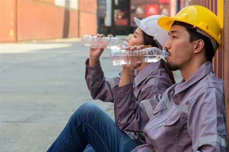Young Asian Man And Woman Engineer Wearing Safety Helmet Drinking Water