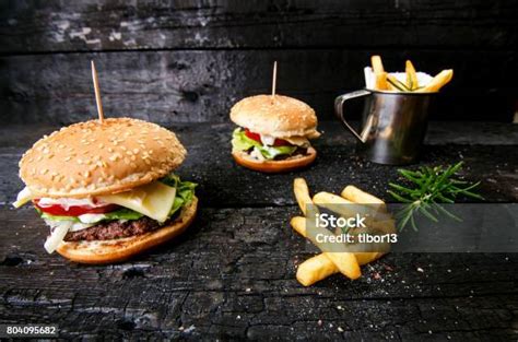 햄버거와 감자 튀김 탄 검은 나무 테이블에 패스트 푸드 식사입니다 집 햄버거를 쇠고기 고기 상 추 토마토 쓰레기통 드레싱 치즈 향신료의 구성 했다 빈티지 감자 요리에 대한