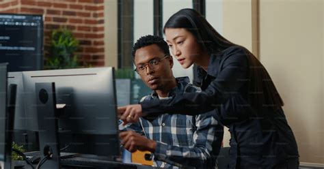 두 명의 소프트웨어 개발자가 책상에 앉아 코딩 인터페이스가 있는 노트북을 들고 컴퓨터 화면을 가리키고 있습니다 프로그래머 팀은