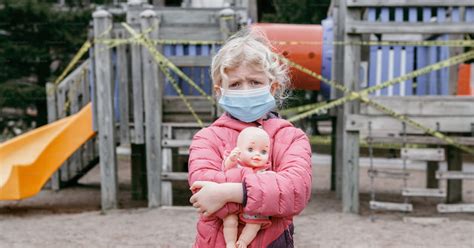 닫힌 놀이터 야외에서 아기 장난감을 가진 얼굴 마스크를 쓴 슬픈 백인 소녀 캐나다 토론토에서 노란색 주의 테이프로 잠긴 어린이 놀이 공간 코로나 바이러스 사회적 거리