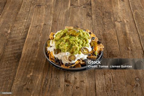 녹은 치즈 피코 데 갈로 과카몰리를 곁들인 나초를 곁들인 둥근 검은 점토 그릇이 유약을 바르지 않은 나무 테이블 위에 있습니다 건강한 생활방식에 대한 스톡 사진 및 기타