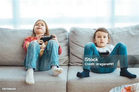 예쁜 어린 소녀와 소년은 집에서 소파에 앉아있는 동안 게임 콘솔과 웃고있다 놀기에 대한 스톡 사진 및 기타 이미지 놀기 놀이 소녀 Istock