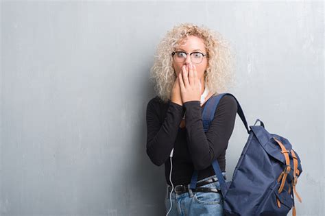 젊은 금발 여자 배낭과 헤드폰 입 실수에 대 한 손으로 다루는 충격된을 입고 그런 지 회색 벽에 비밀 개념입니다 가리기에 대한 스톡 사진 및 기타 이미지 Istock