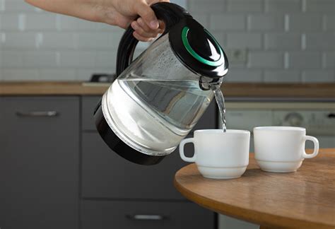 주방의 나무 테이블에 있는 현대적인 전기 투명 주전자 물을 끓이고 차를 만들기위한 주전자 뜨거운 음료를 만들기위한 가전 제품 복사 공간 텍스트를 위한 장소입니다 가정 생활에