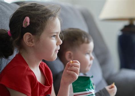 Premium Photo Brother And Sister Are Eating Chips And Watching An