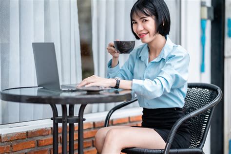 치과 교정기로 미소 짓는 아시아 프리랜서 사업가들은 커피숍에서 노트북과 스마트폰이 있는 노트북 컴퓨터와 함께 일하는 커피잔