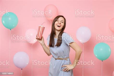 블루 드레스를 입고 화려한 공기 풍선 파스텔 핑크 배경에 소 다 또는 콜라의 플라스틱 컵을 들고 웃는 젊은 예쁜 여자의 초상화 생일 휴가 파티 사람들이 진심으 감정 개념