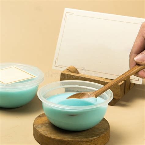 A Hand Holds A Wooden Spoon Mixing A Vibrant Blue Bubble Gum Pudding In A Bowl Against A Neutral