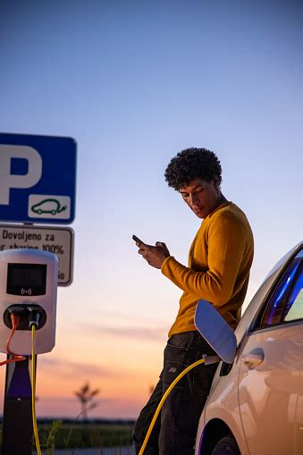 전기 자동차를 충전하는 동안 휴대 전화를 사용하는 남자 전기 자동차 대체 연료 자동차에 대한 스톡 사진 및 기타 이미지 전기 자동차 대체 연료 자동차 차 전기자동차