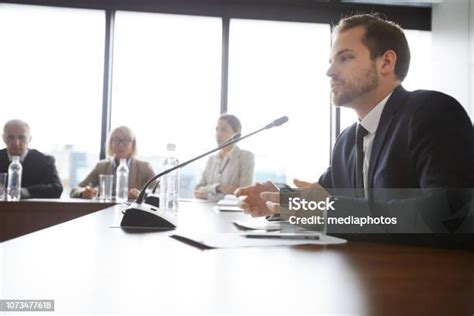 벌 나무 테이블에 앉아 및 개발의 계획 회의에서 기자 들과 공유 하는 동안 마이크에 말하기에 심각한 자신감 잘생긴 젊은 사업가