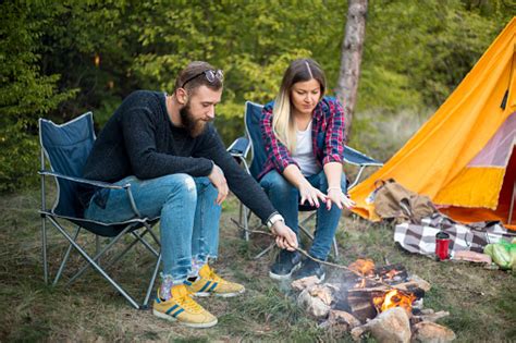 아름 다운 커플 앉아 캠프 파이어 주위에 캠핑 텐트와 배경에 남자 막대기로 화재 제스처 건강한 생활방식에 대한 스톡 사진 및 기타 이미지 Istock