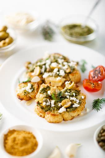 채식 음식 개념 향신료 치미추리 소스 아몬드 플레이크 올리브 튀긴 체리 토마토 케이퍼가 있는 콜리플라워 스테이크를 화이트 플레이트에 얹습니다 흰색 배경입니다 0명에 대한