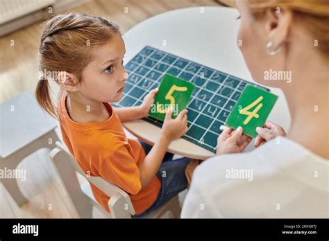 Clever Girl And Teacher Holding Numbers Near Chalkboard Learning