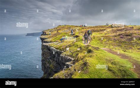 Group Of Tourists Hiking And Sightseeing Iconic Cliffs Of Moher