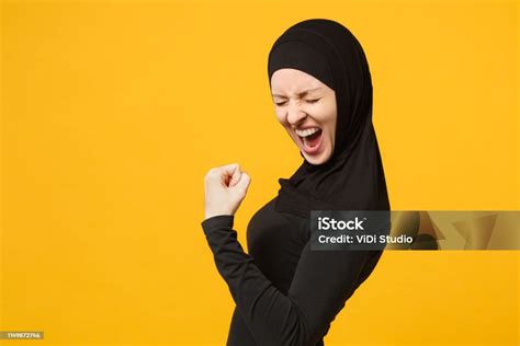 과다 한 젊은 아라비아 무슬림 여 자가 히 잡 검은 옷을 하 고 위 너 제스처를 하 고 예 노란 벽 배경 스튜디오 초상화에 고립 된 말 사람들 종교적 라이프 스타일