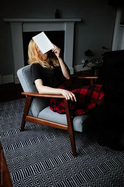 Woman Sitting In A Room With A Book Covering Her Face By Stocksy