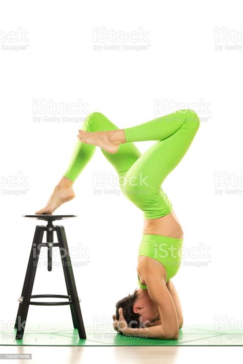 하얀 스튜디오에서 요가를하는 녹색 운동복을 입은 아름다운 젊은 여성 의자와 함께지지 헤드 스탠드에 서서 Salamba Sirsasana 전체 길이 측면보기 30 34세에